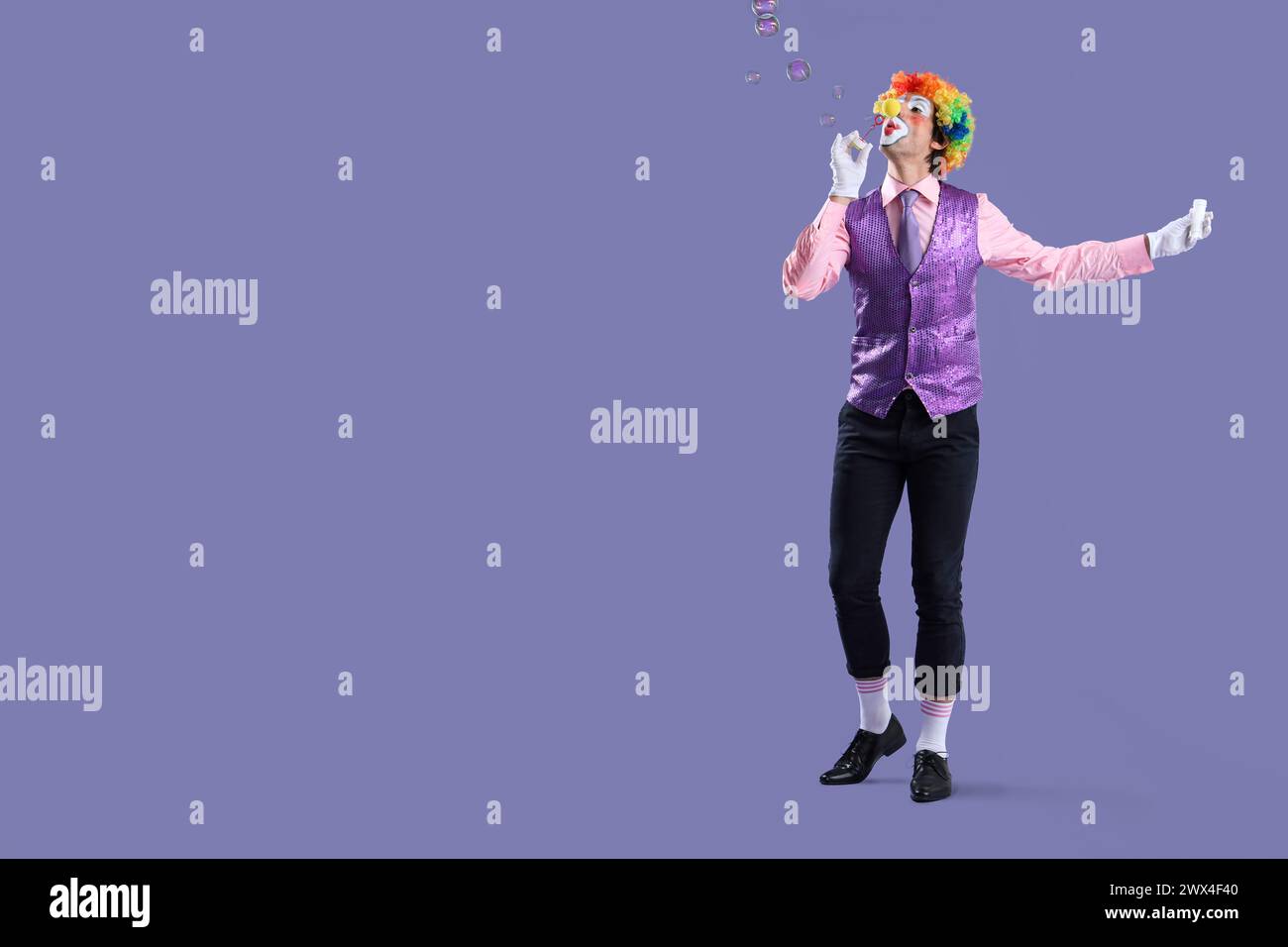 Portrait of clown blowing soap bubbles on lilac background. April Fool ...
