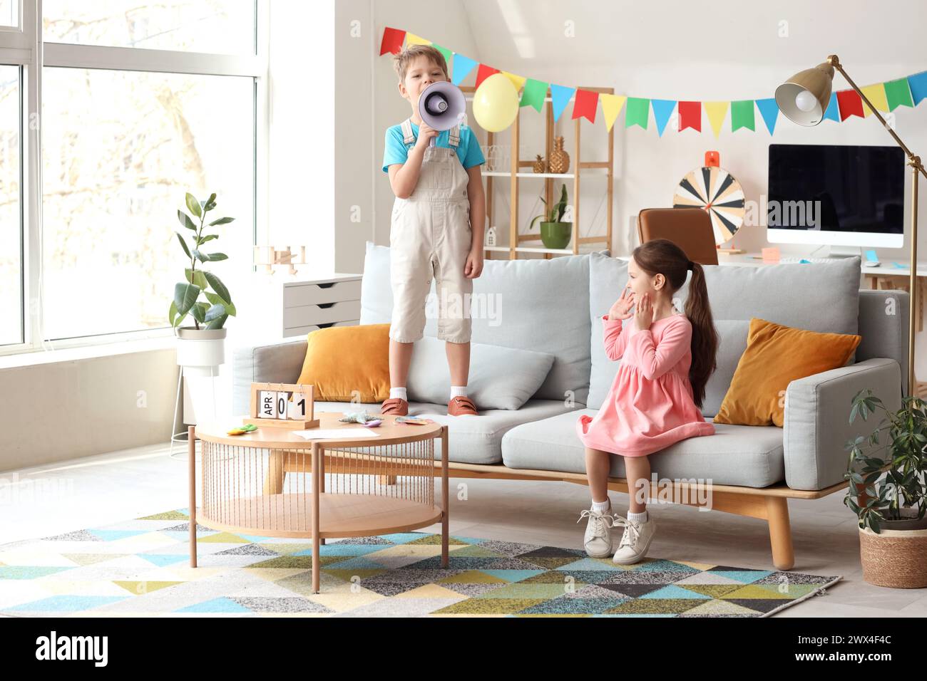 Cute little boy scaring his sister with megaphone at home. April Fool's ...