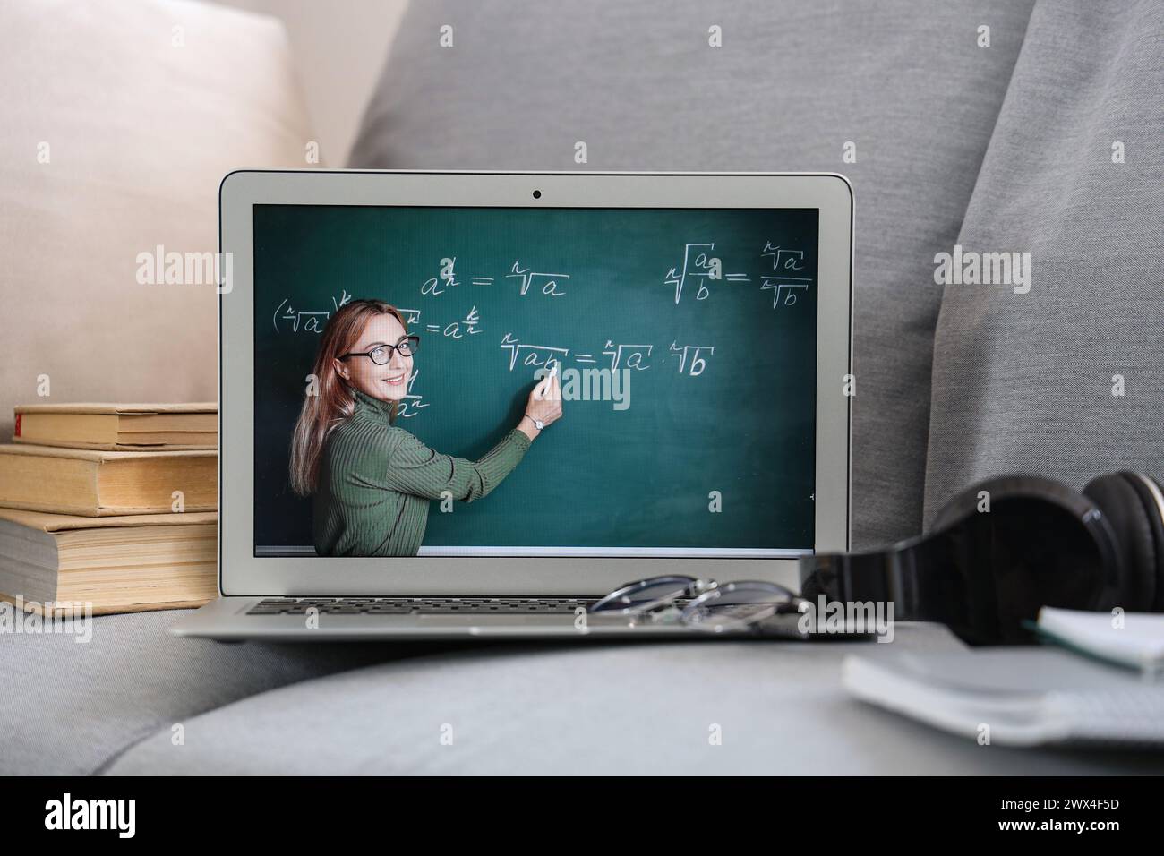 Screen of laptop with Math teacher giving online lesson on sofa in room ...