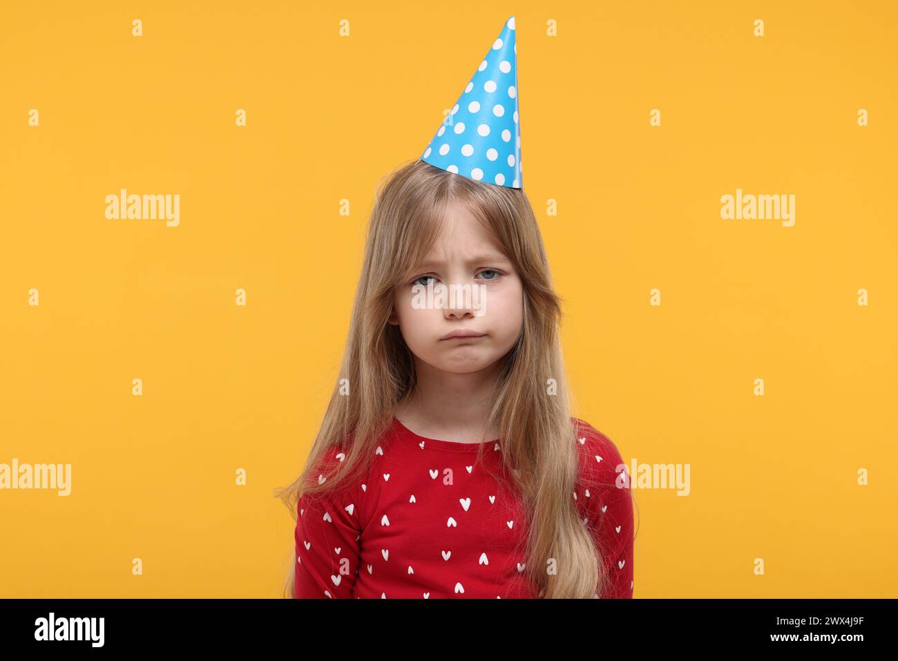Unhappy little girl in party hat on yellow background Stock Photo - Alamy