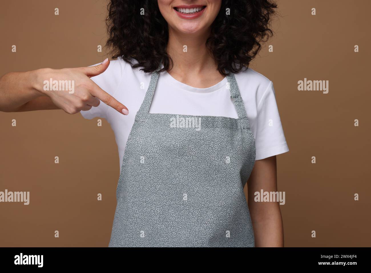 Woman pointing at kitchen apron on brown background, closeup. Mockup ...