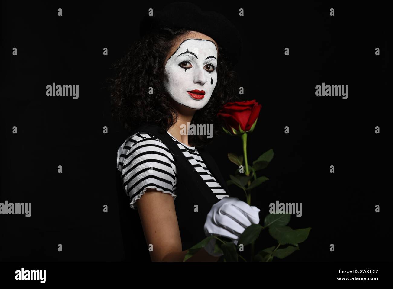 Young woman in mime costume with red rose posing on black background ...