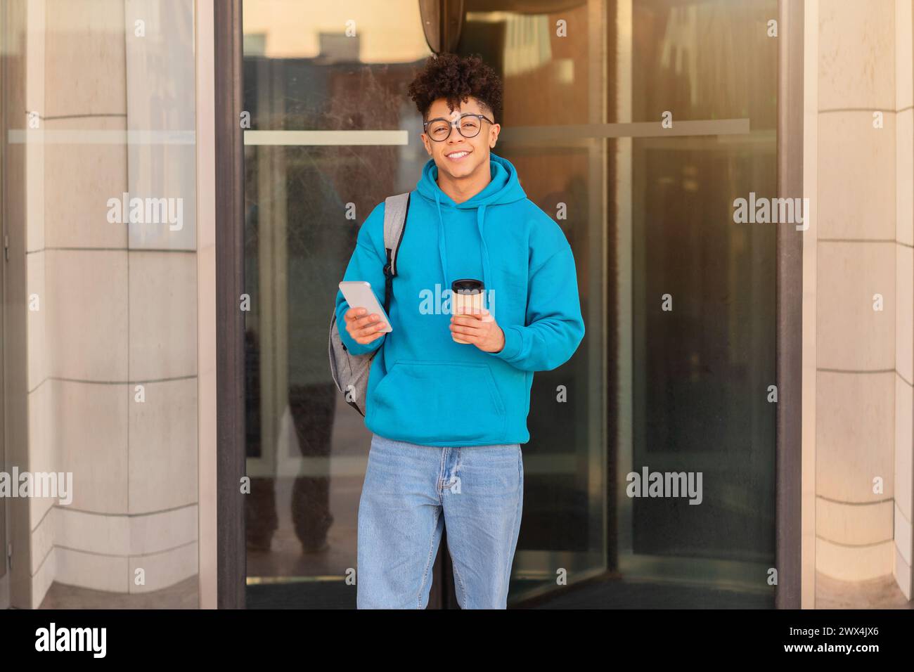 Student with phone and coffee entering building Stock Photo - Alamy