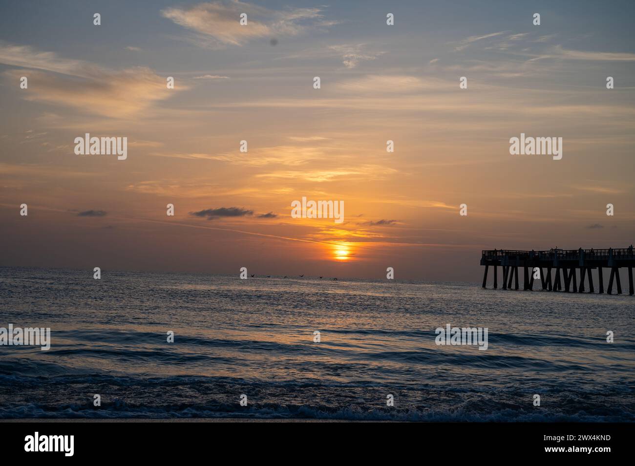Sunset over ocean with distant pier Stock Photo - Alamy