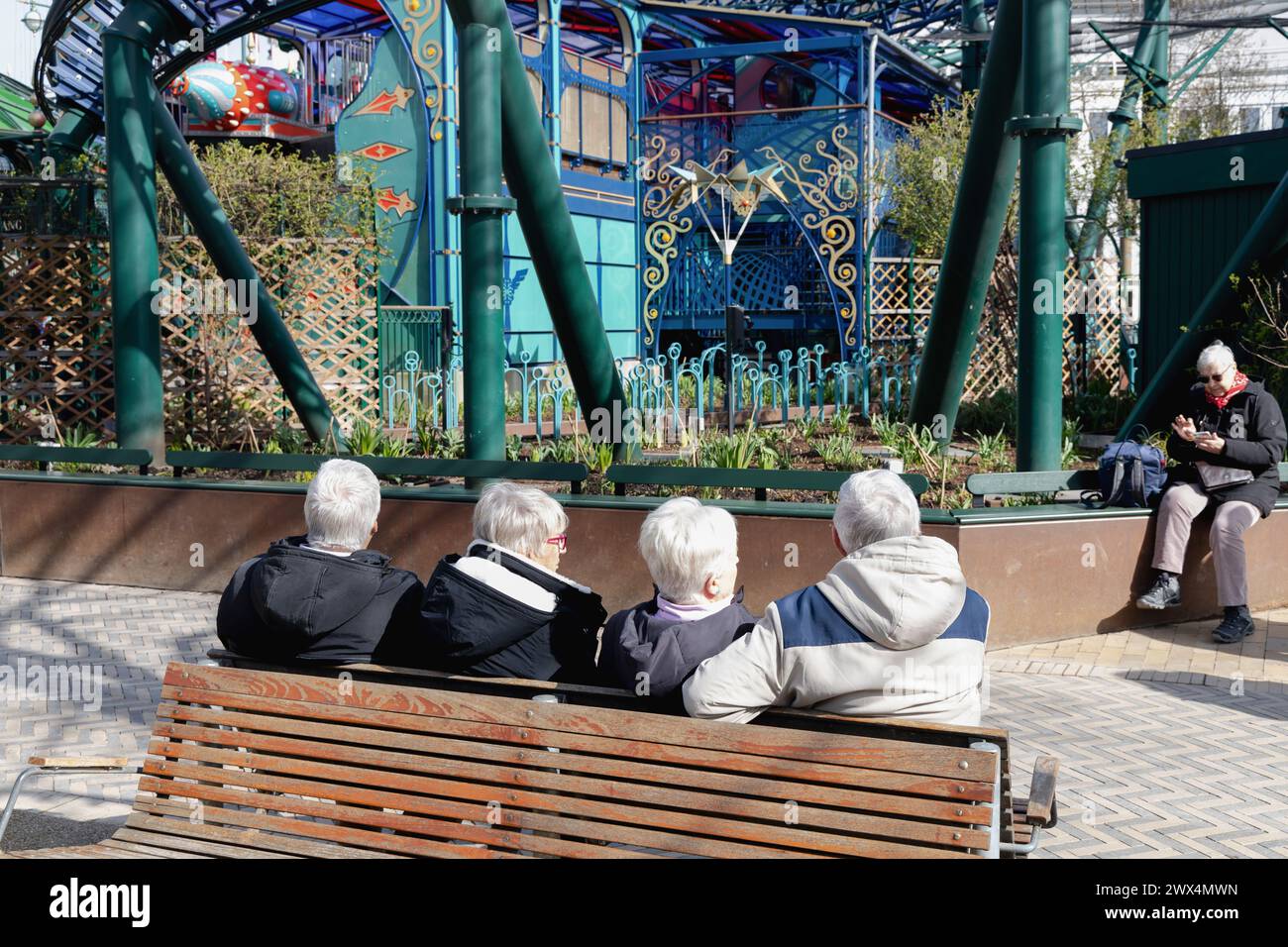 Four elderly people with gray hair are sitting and relaxing on a bench ...