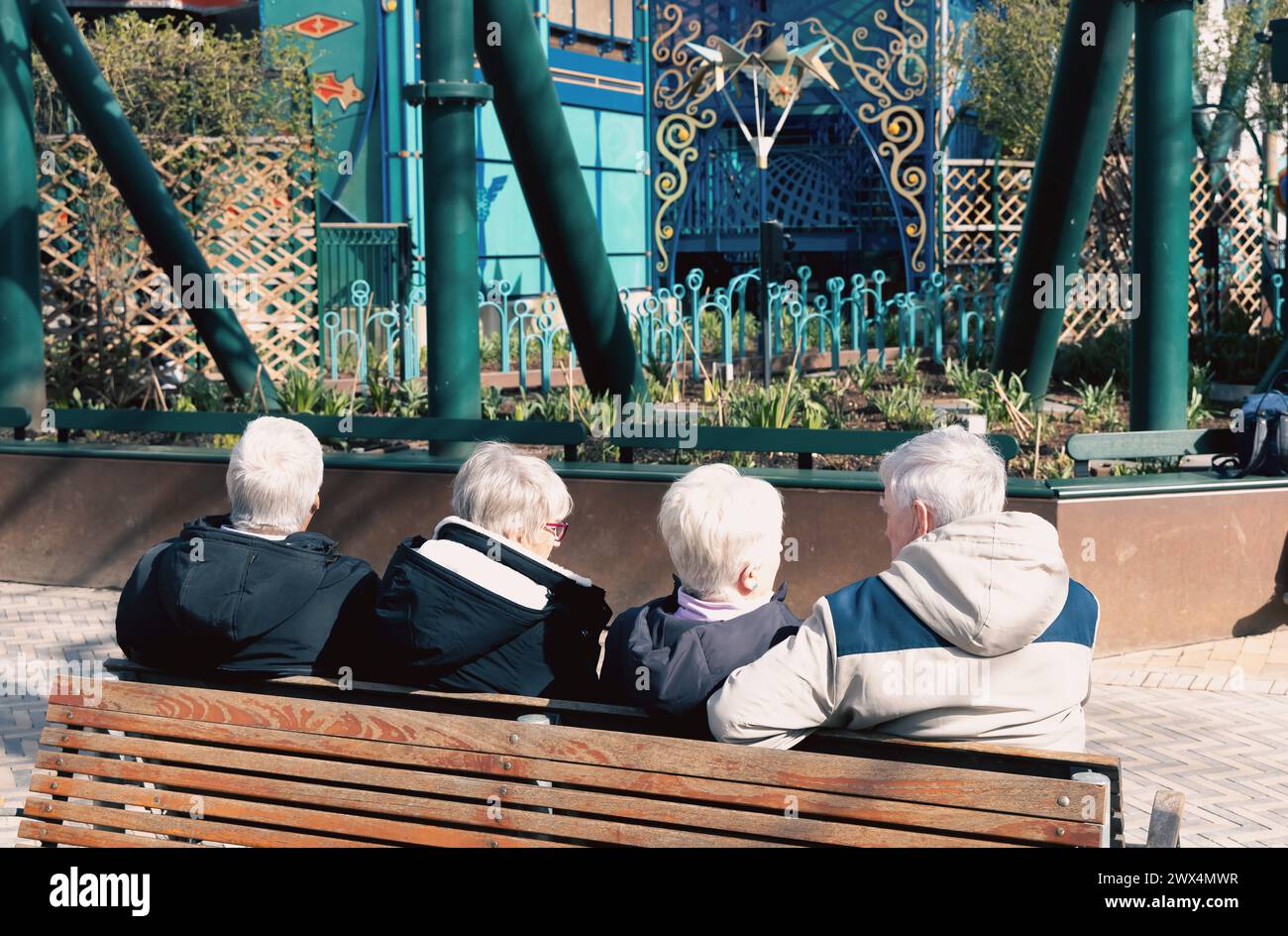 Four elderly people with gray hair are sitting and relaxing on a bench ...