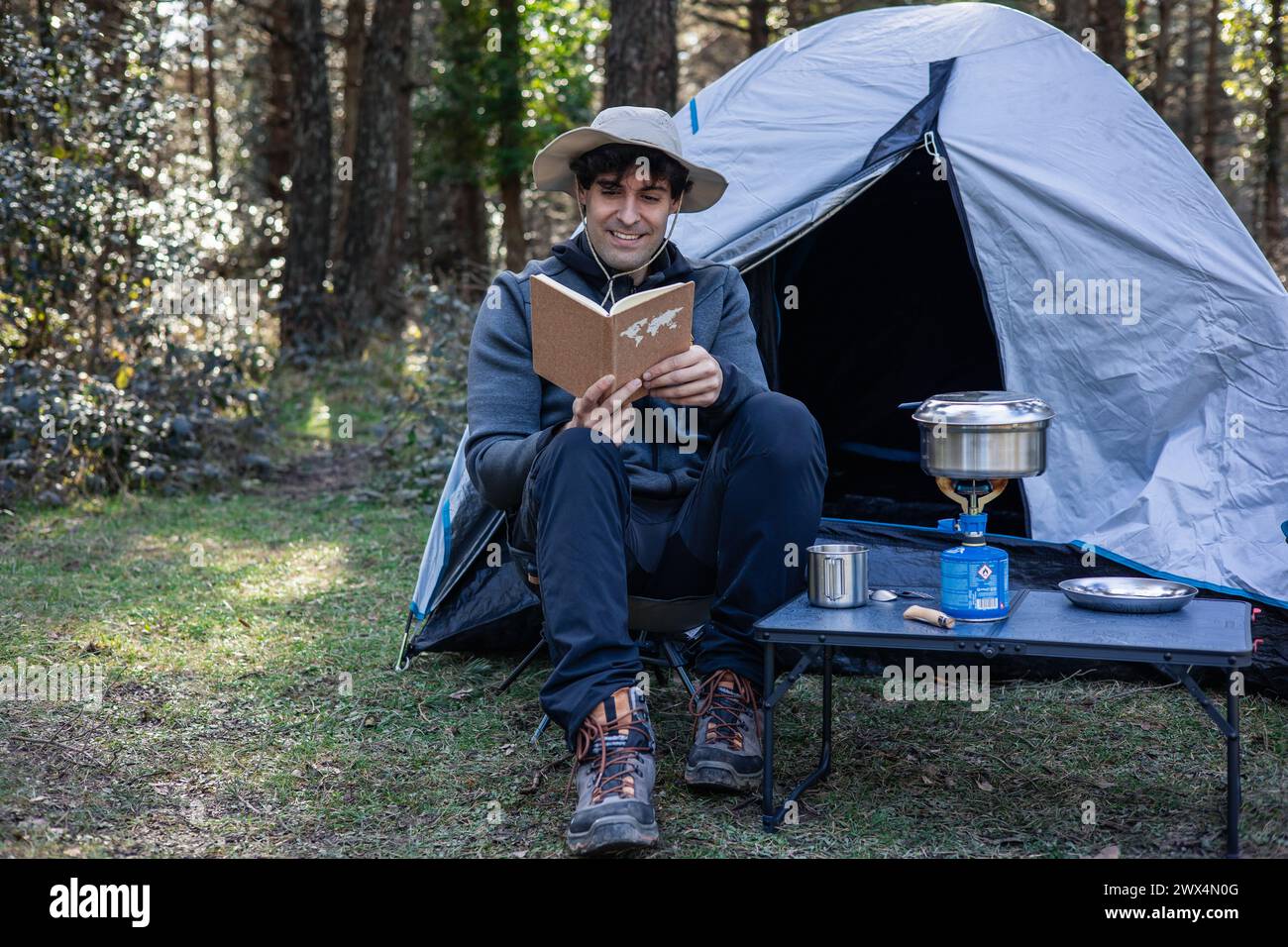 Adventurous man wearing an explorer hat enjoying a book at his forest ...