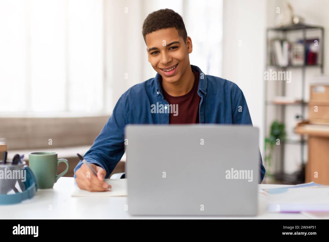 Smiling man writing notes with laptop Stock Photo - Alamy