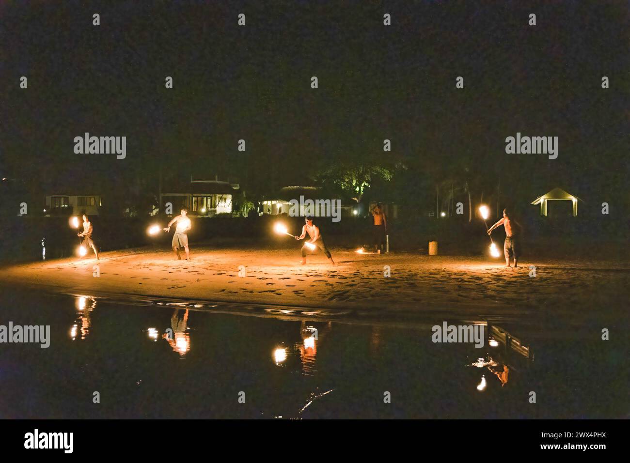 A group of fire dancers perform on a sandy part of a lagoon, on Koh ...