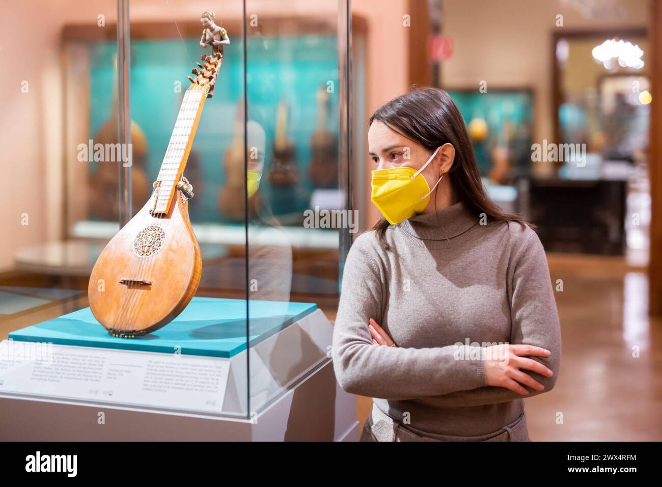 Female museum visitor in mask examining ancient musical instruments ...