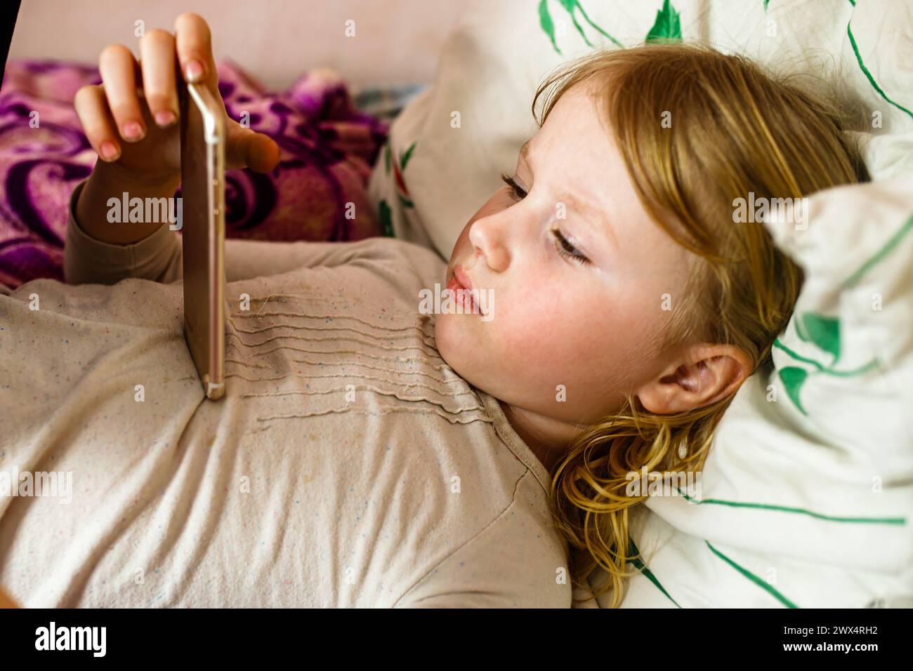 Little girl lying in bed with a mobile phone in her hand Stock Photo ...