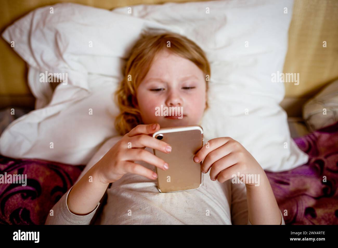 Little girl lying in bed and using mobile phone. Focus on smartphone ...
