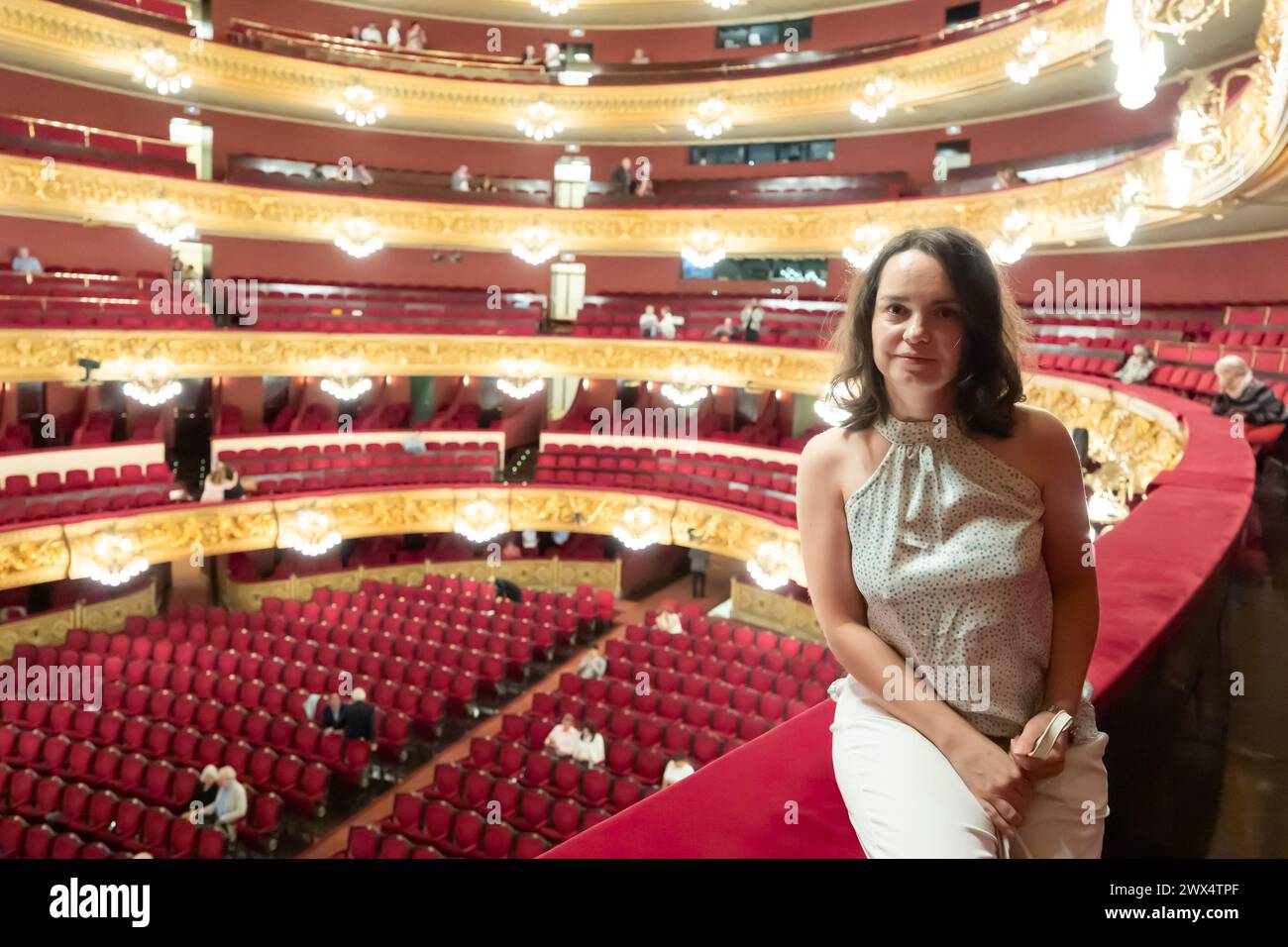 Interested young adult brunette sitting on balcony of classic concert ...
