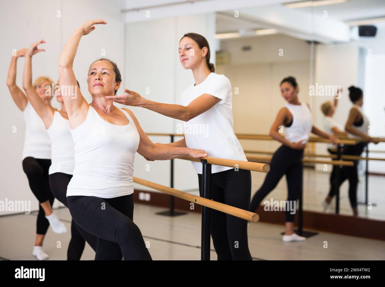Female ballet trainer teaching group of dancers near ballet barre in ...