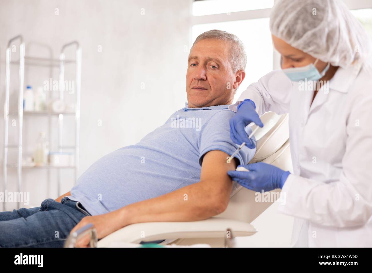 Elderly man getting intramuscular injection in upper arm in medical ...