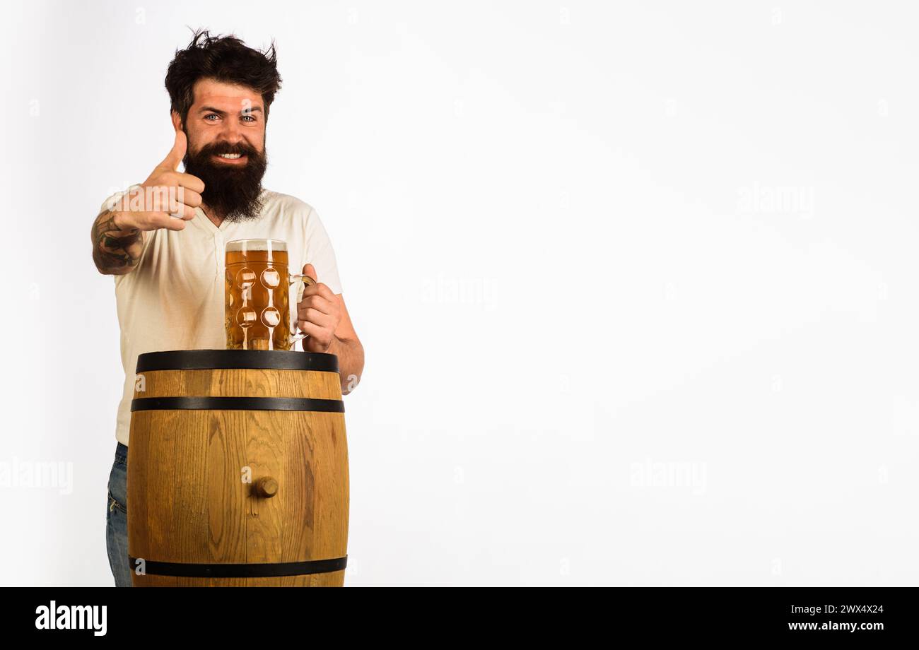 Beer time. Bearded man with mug of beer on wooden barrel showing thumb ...