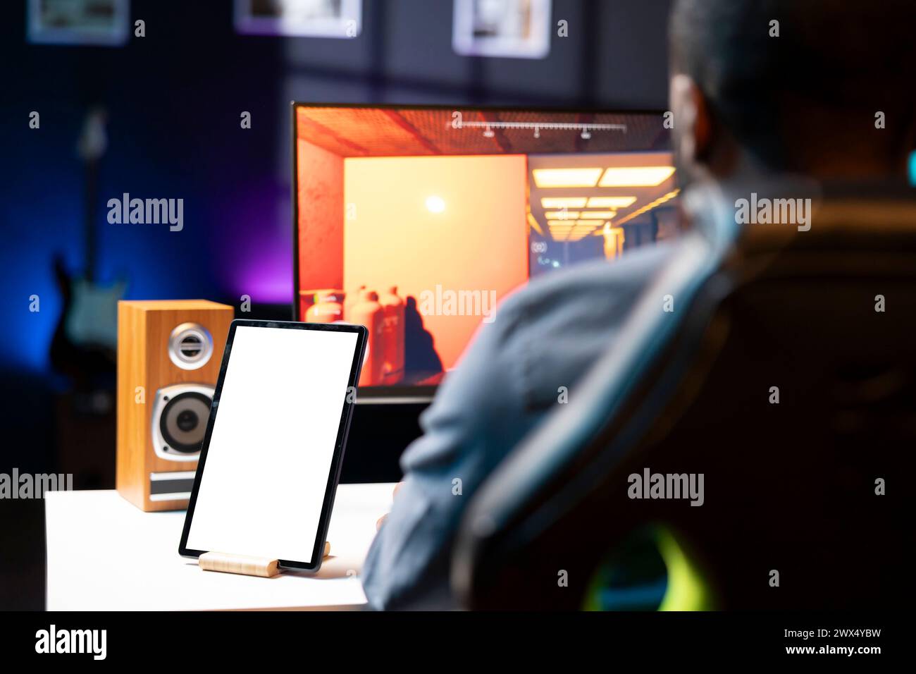 Mockup tablet on desk next to man in dark living room playing videogame ...