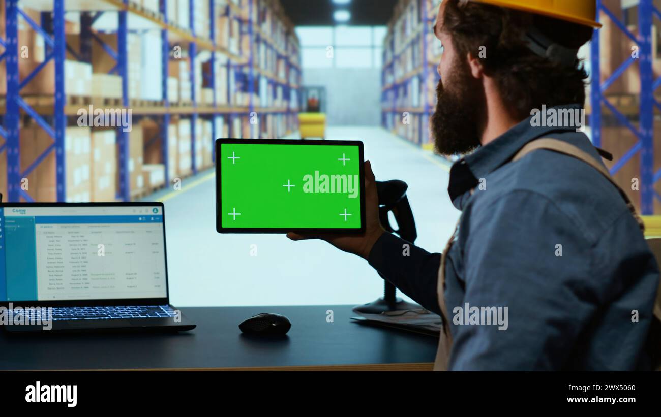 Packaging engineer looking at tablet with greenscreen in depot, working ...