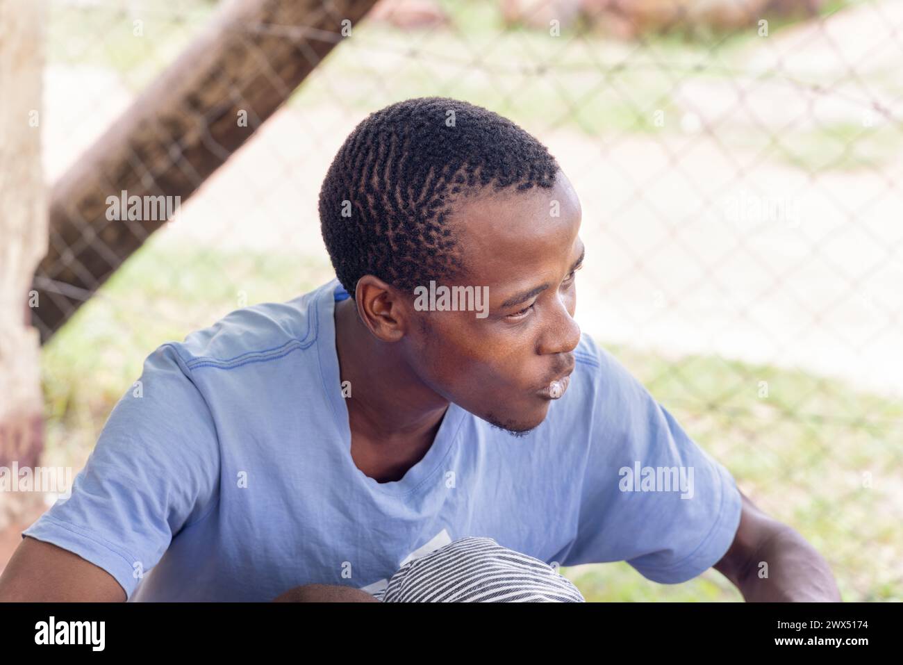 portrait of young african man, sited in the yard in front of the house ...