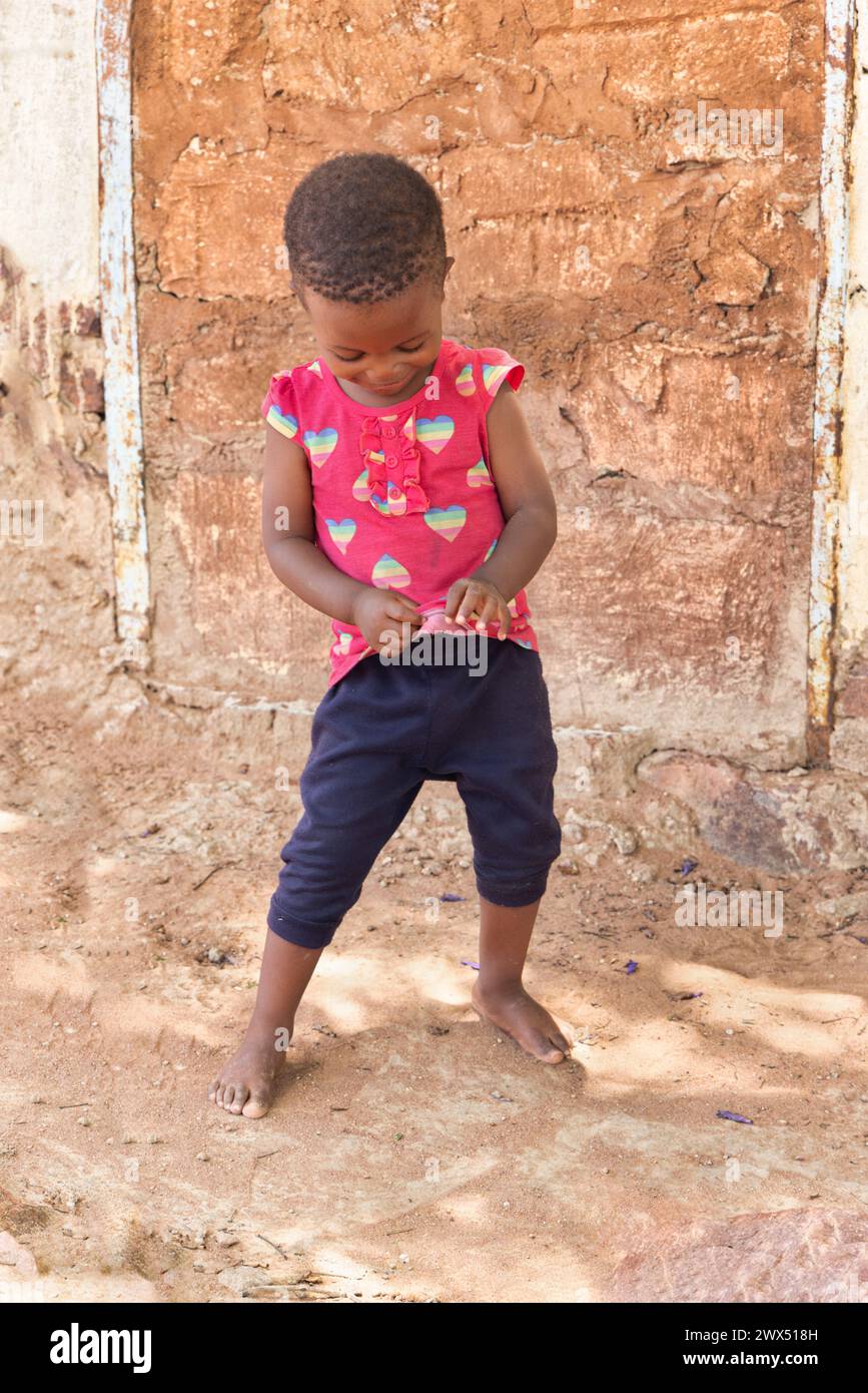 single african villager child playing outdoors in front of the house in ...