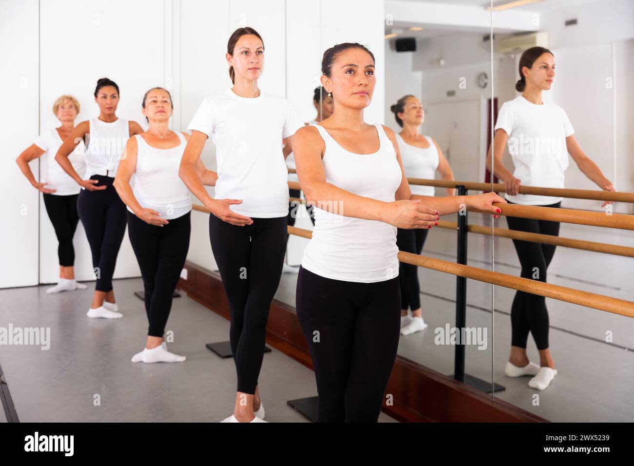 Group of women engaged in classical ballet stand holding onto a barre ...