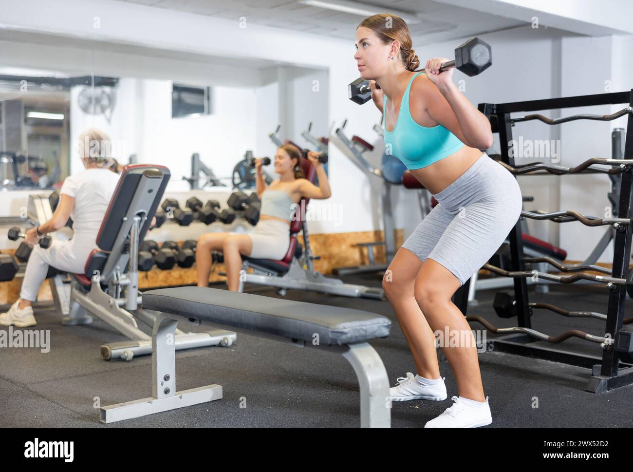 Slender girl trains muscles of arms and back using barbell and ...