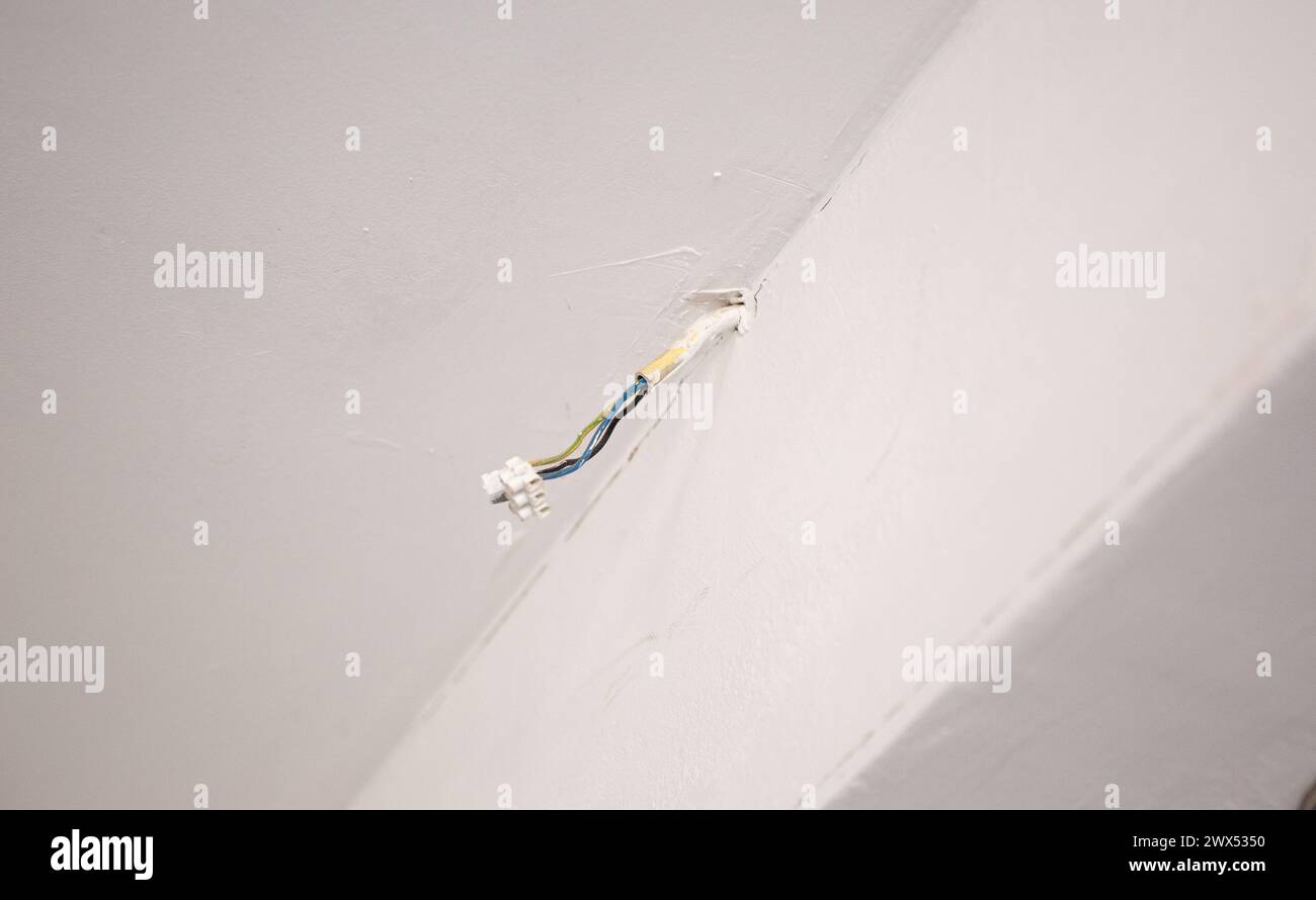 An electrical cable hanging out of a white wall Stock Photo - Alamy