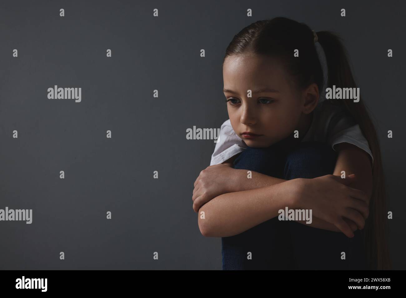 Sad girl sitting near dark grey background, space for text Stock Photo ...