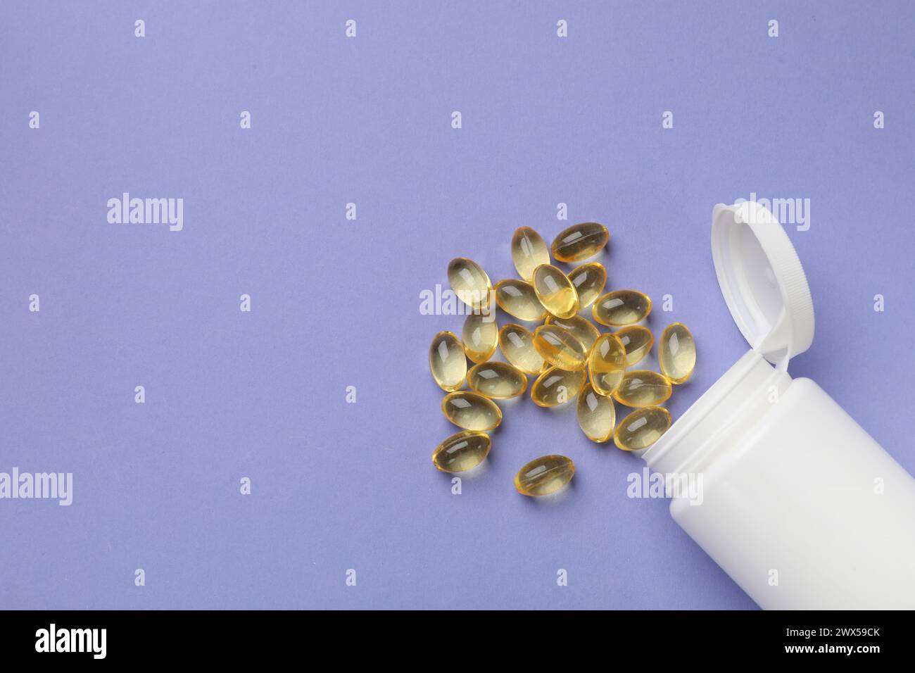 White bottle and vitamin capsules on violet background, top view. Space ...