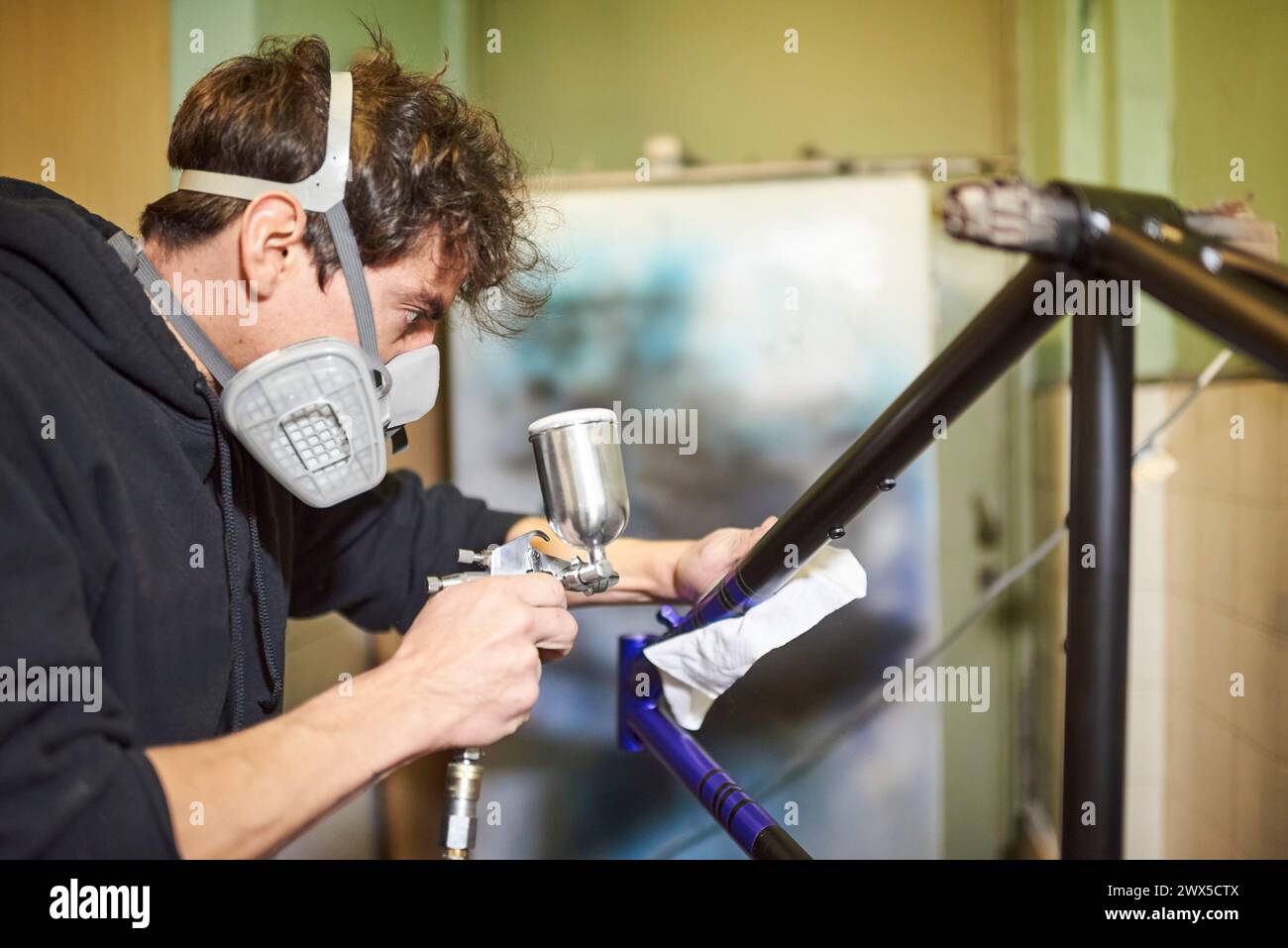 Latin young man wearing a respirator mask concentrated spray painting a ...