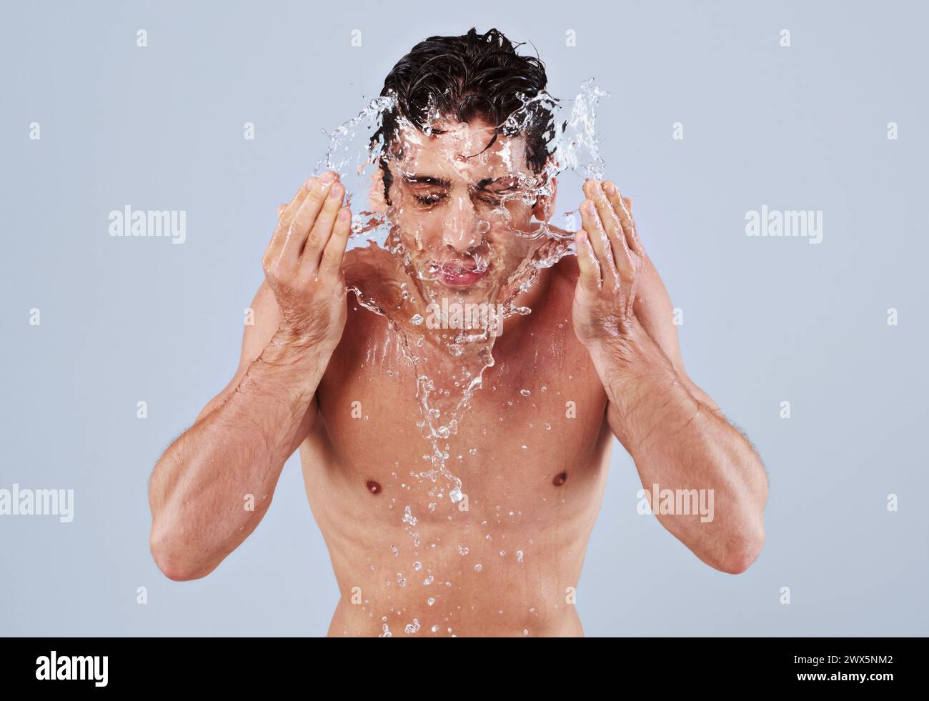 Water splash, washing face and man on blue background for skincare, wellness and cleaning in ...