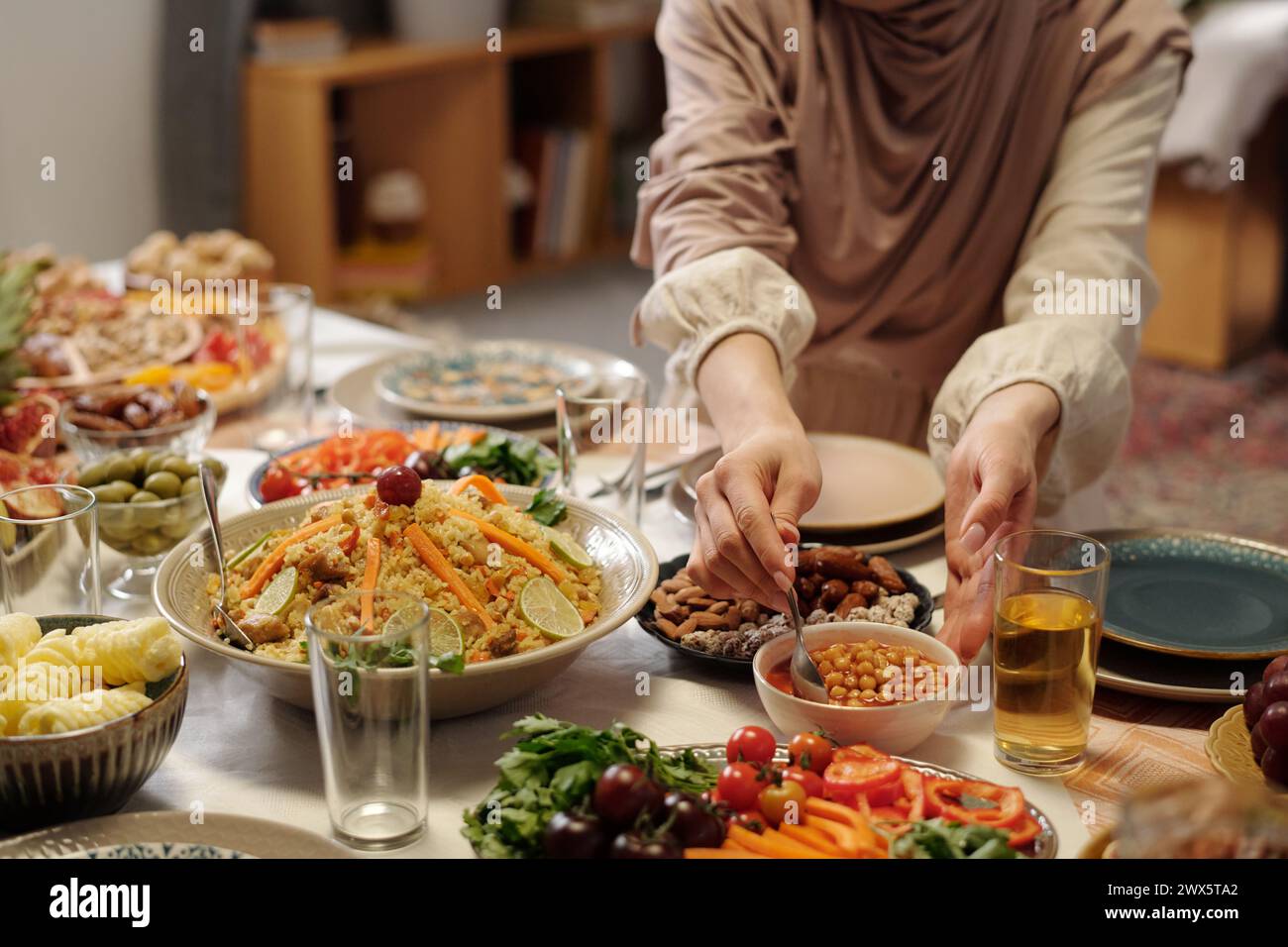Unrecognizable young Muslim woman wearing hijab setting festive table ...