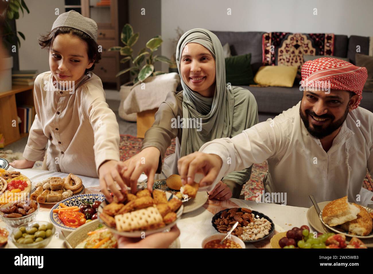 Happy Muslim man, woman and kid taking desserts from plate ...