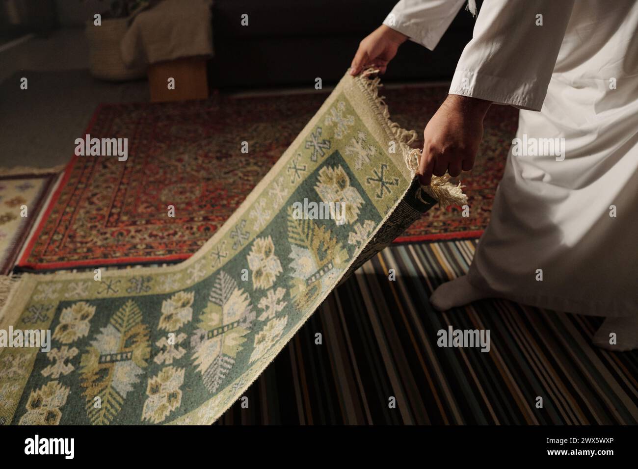 Unrecognizable Muslim man placing prayer rug on floor in living room at ...