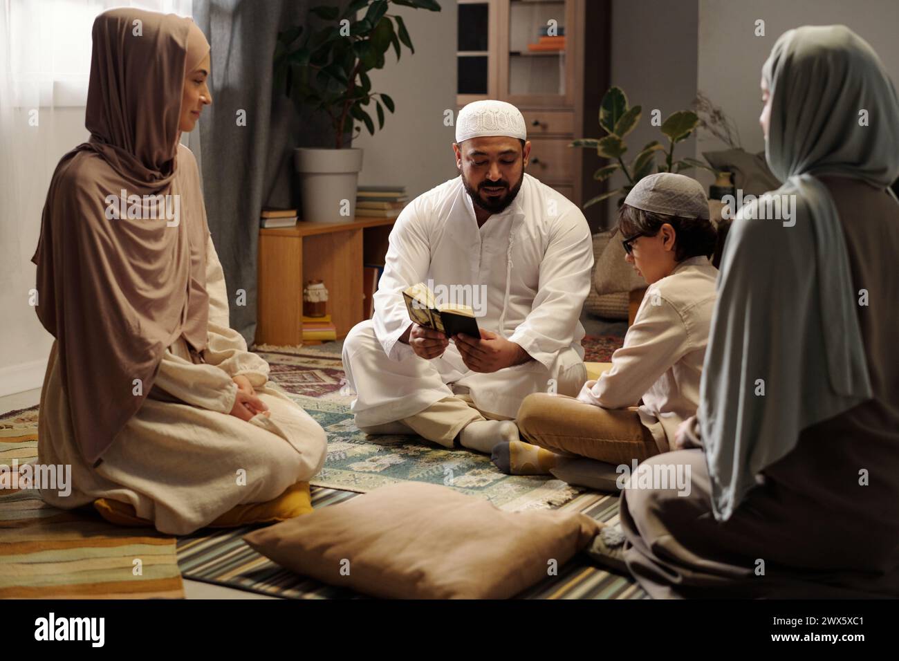 Mature Muslim man sitting on floor in living room reading Quran at ...