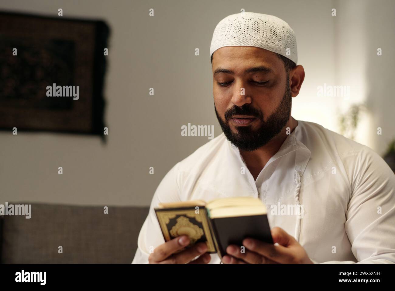 Medium closeup of bearded Muslim man wearing white taqiyah reading holy ...