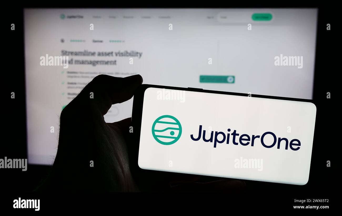 Person holding smartphone with logo of cloud infrastructure management company JupiterOne Inc ...