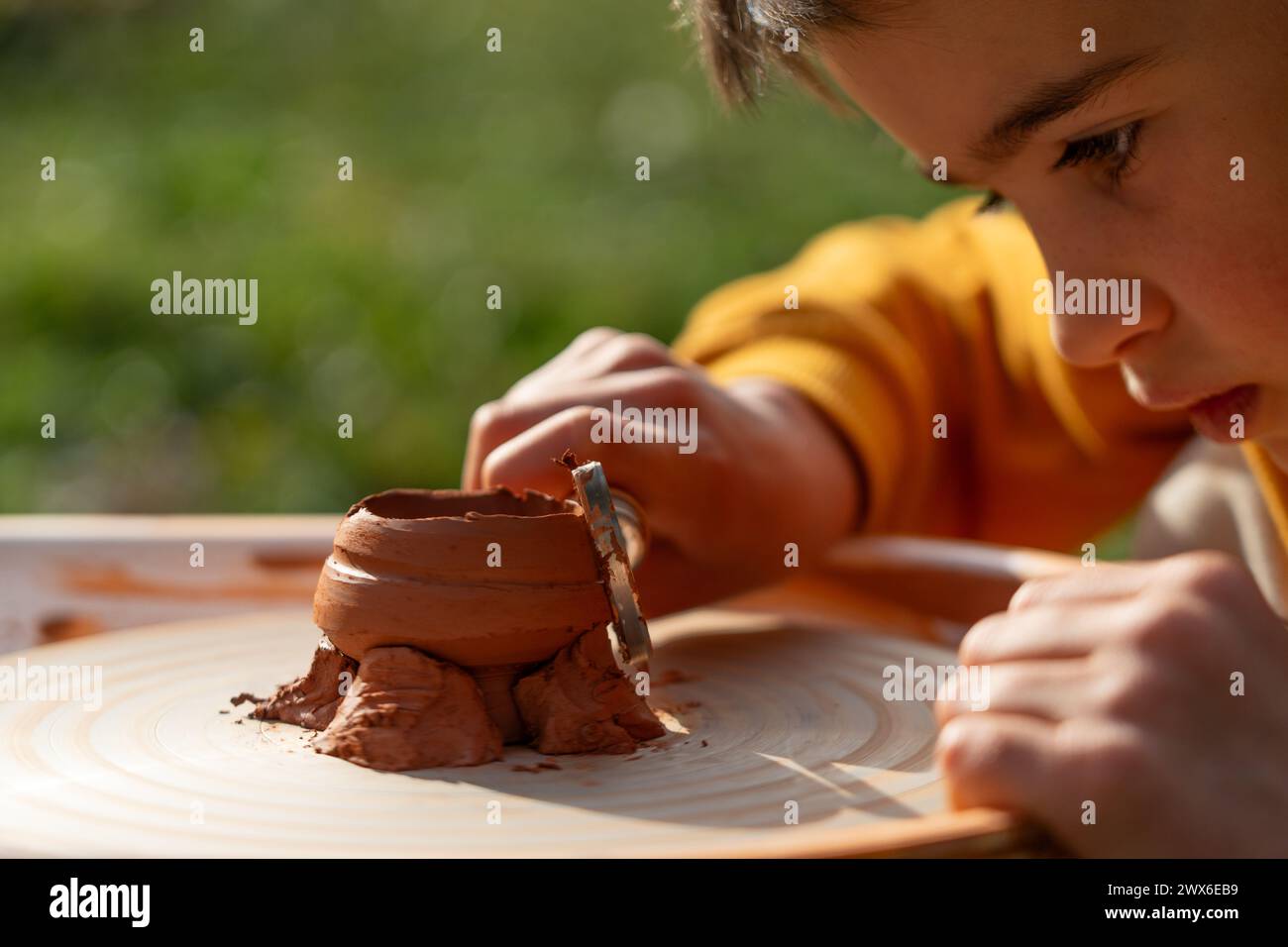 Boy molding clay with a pottery tool on an outdoor potter's wheel Stock ...