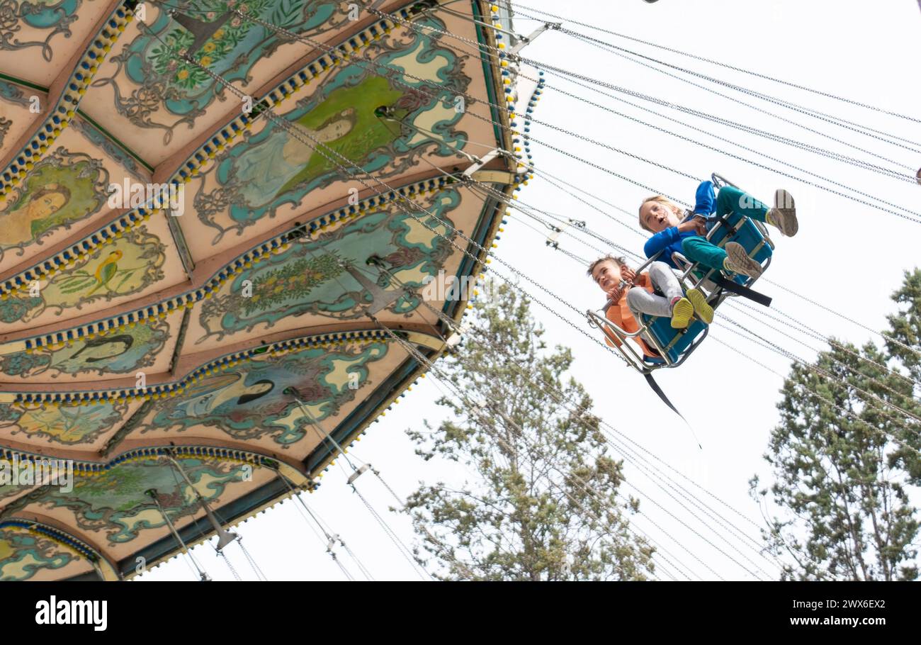 Two children riding a flying swing attraction at an amusement park with ...