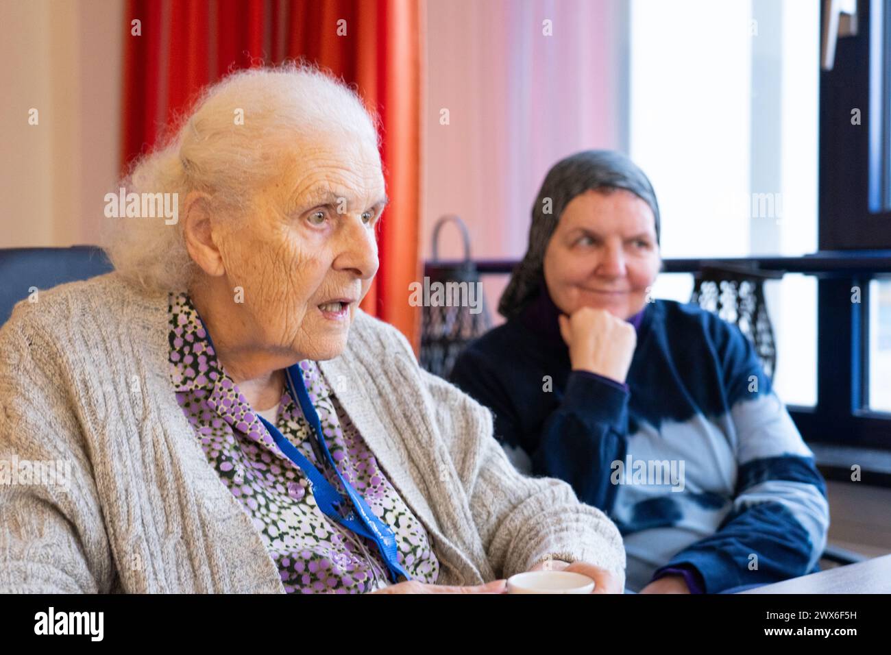 Elderly mother and daughter sitting together looking at something, one ...