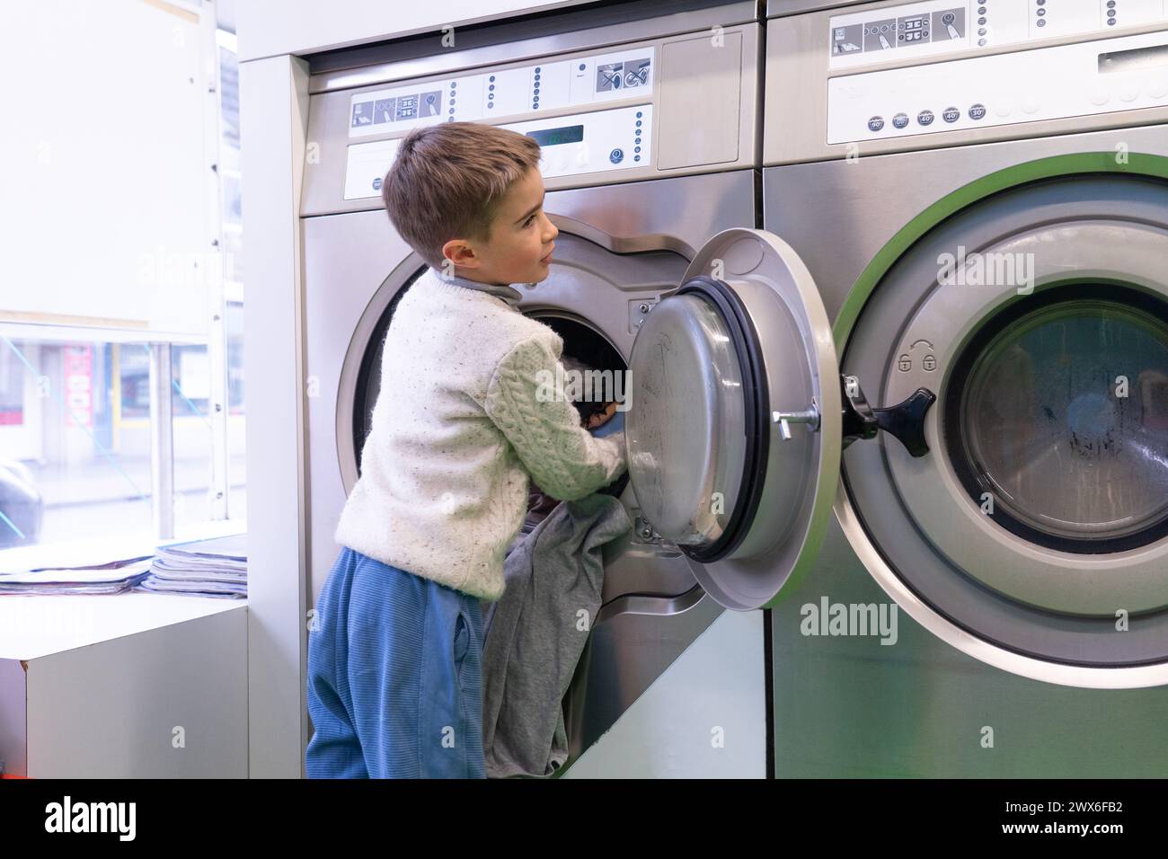 Caucasian boy putting a washing machine in a laundromat doing laundry ...