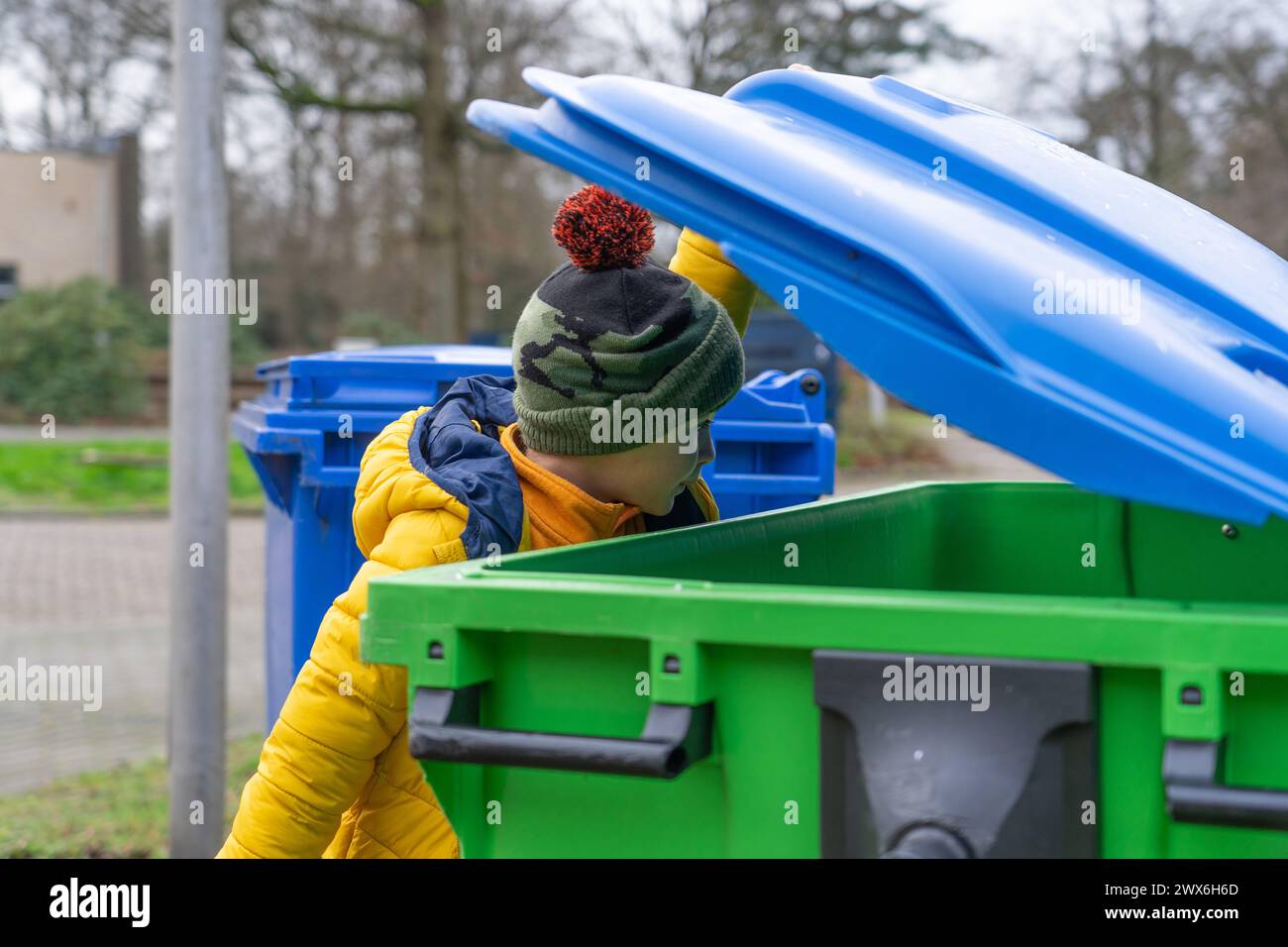 Boy throwing something into a garbage container and looking inside ...