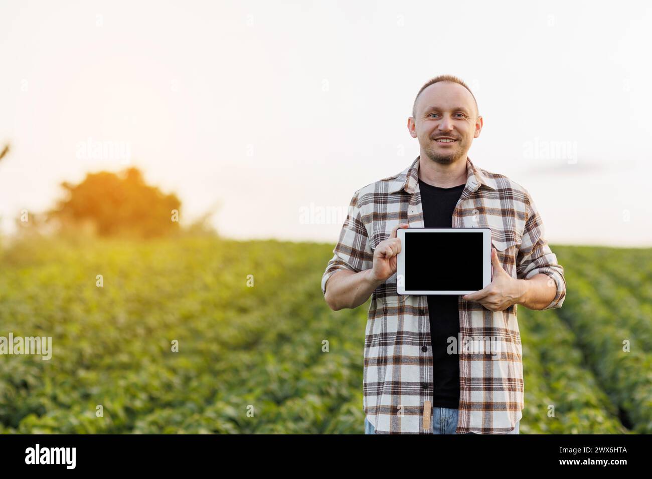 Male farmer shows digital tablet with empty black screen on green ...