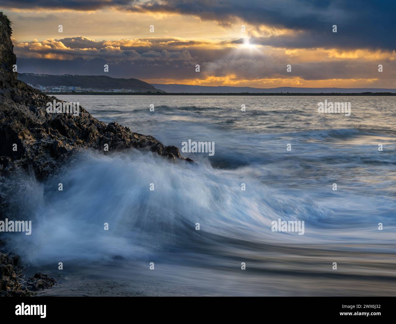 Waves crash against the jagged rocks along the coastal footpath at high ...