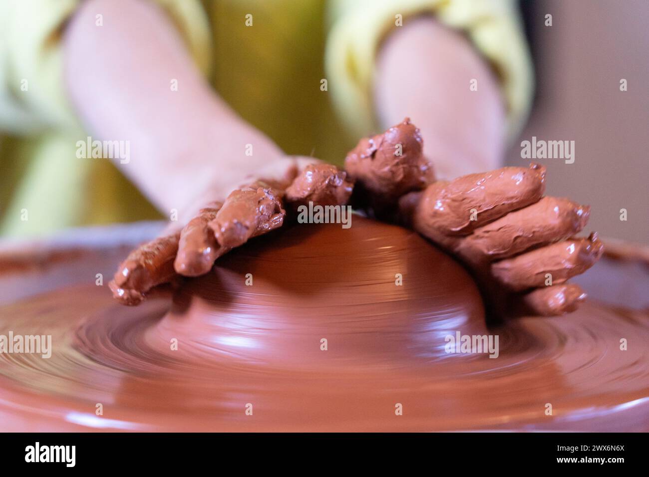 Clay-stained child's hands molding pottery on a wheel viewed from close ...