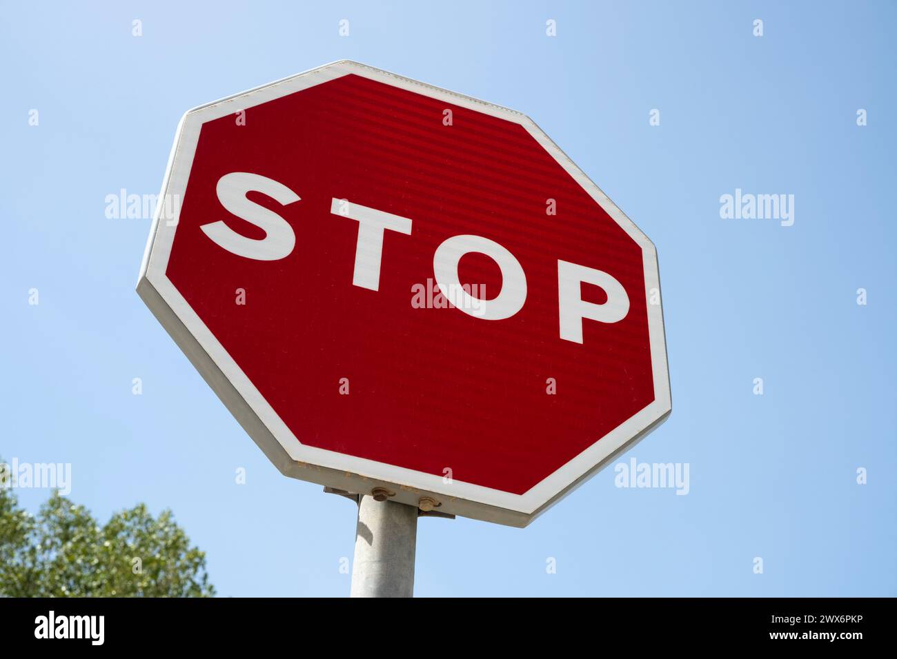 Low angle view of a red Spanish STOP road sign, against a clear blue ...