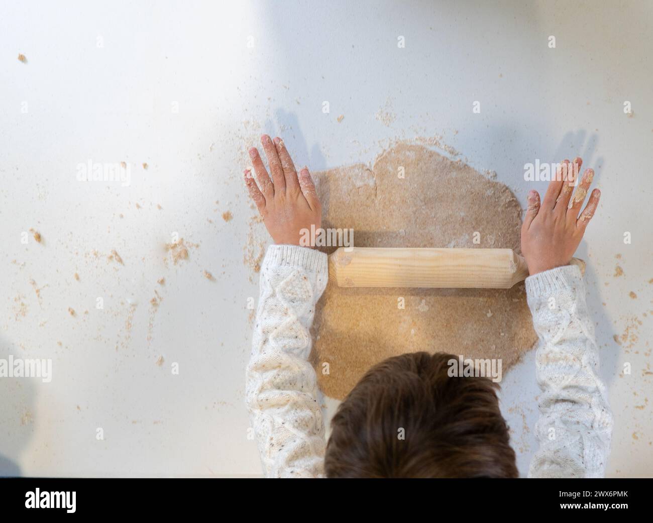 Boy stretching pizza dough with a rolling pin in the kitchen seen from ...