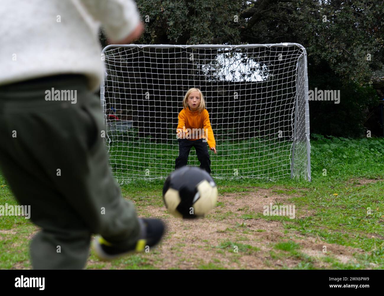 Boy throwing soccer ball at goal and another boy goalkeeper waiting to ...