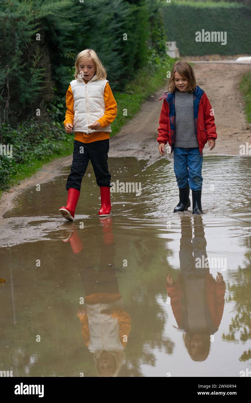Two children walking through a puddle with wellies Stock Photo - Alamy
