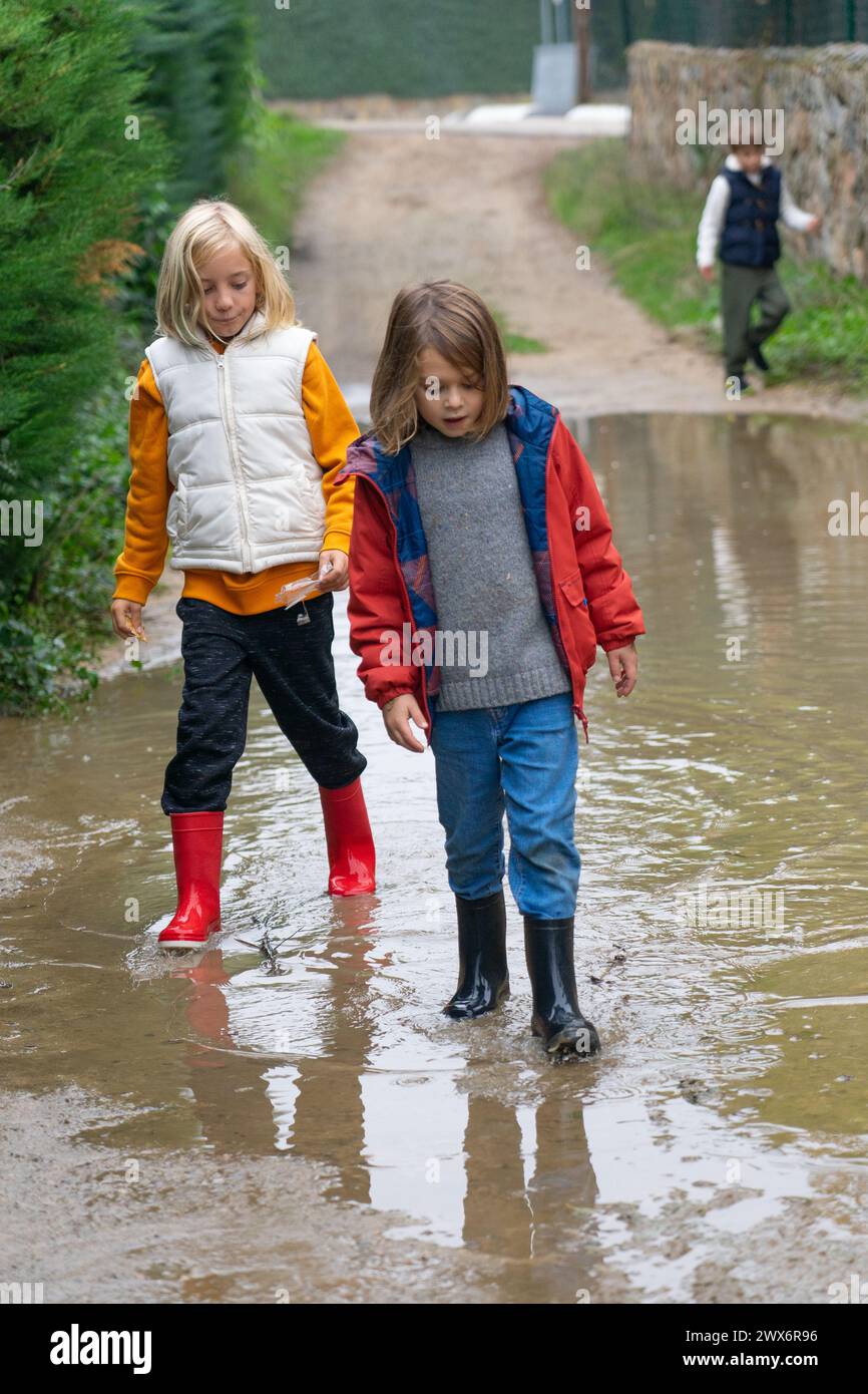 Two children walking over a puddle Stock Photo - Alamy